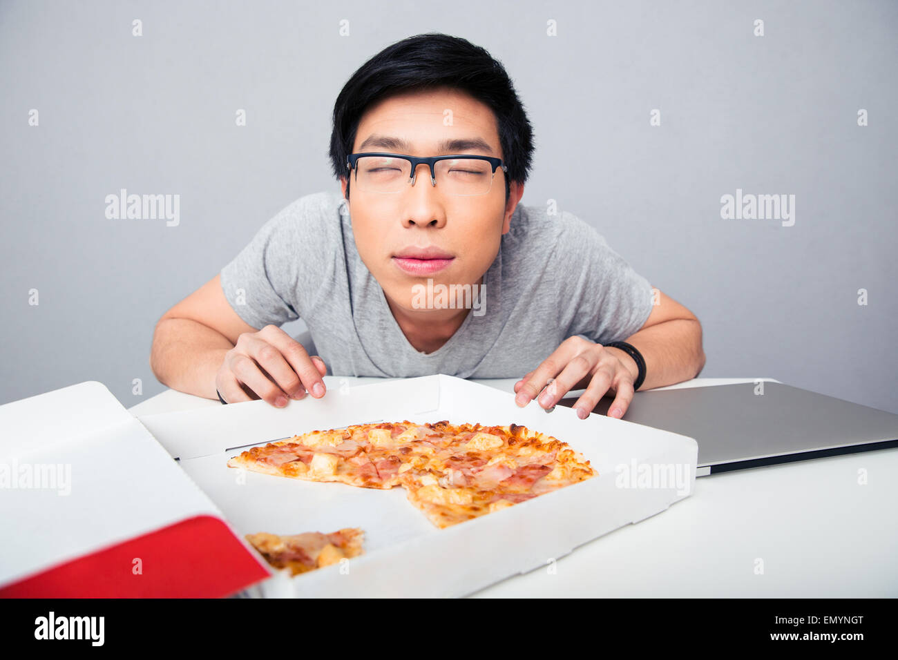 Young asian man sitting at the table and smelling pizza Stock Photo - Alamy