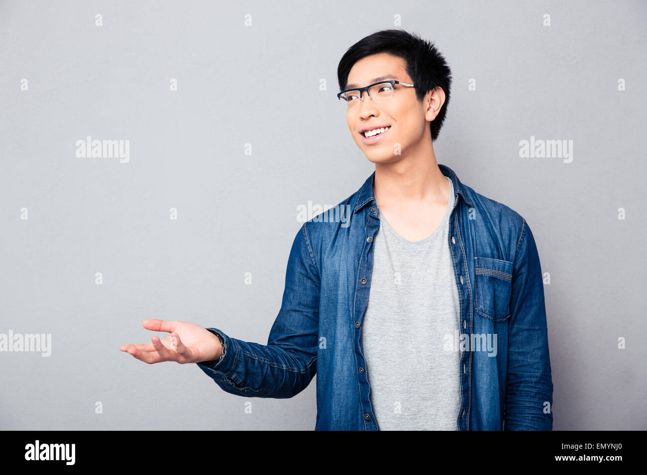 Happy asian man telling something and gesturing with hand over gray ...