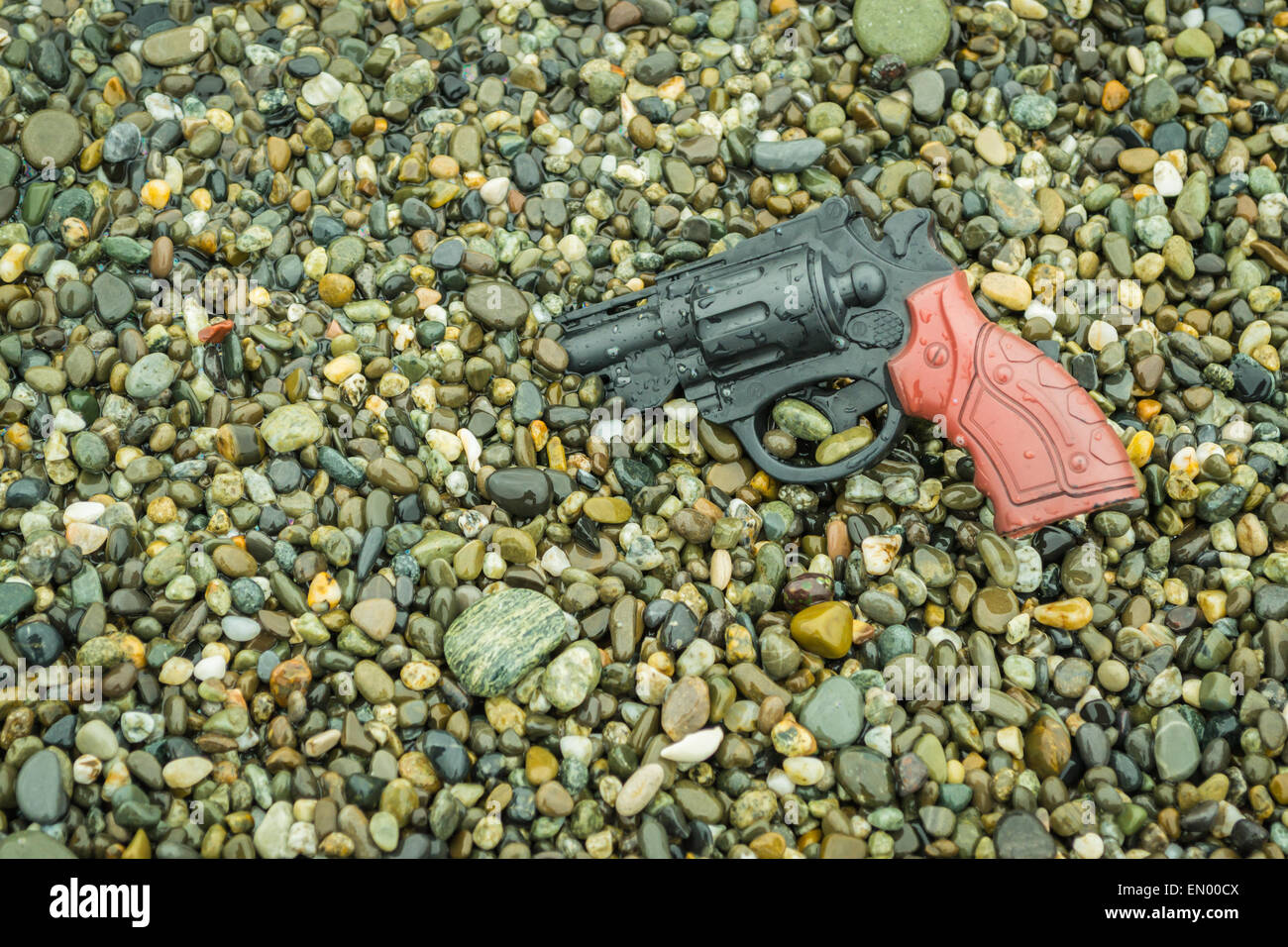 A black and brown gun is buried into stones that are covered in rain ...