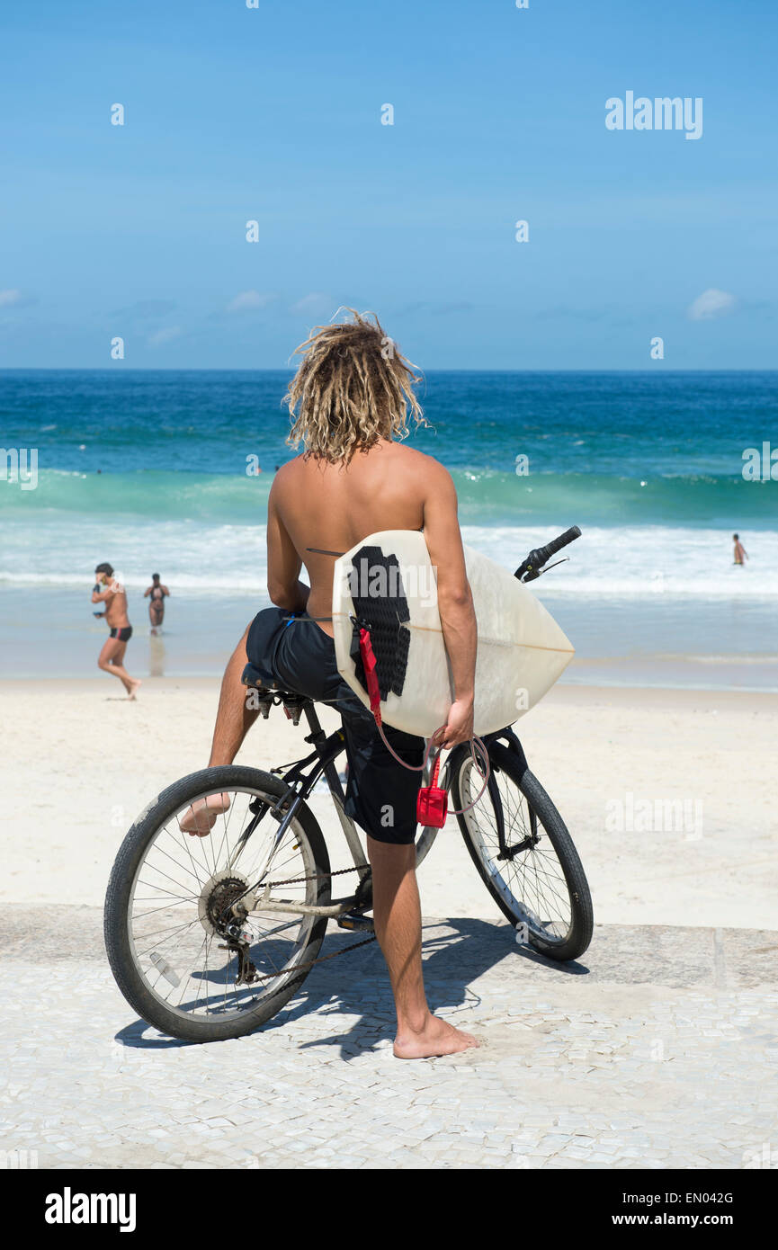 Brazilian surfer on a bike sitting on bike looking out at the waves ...
