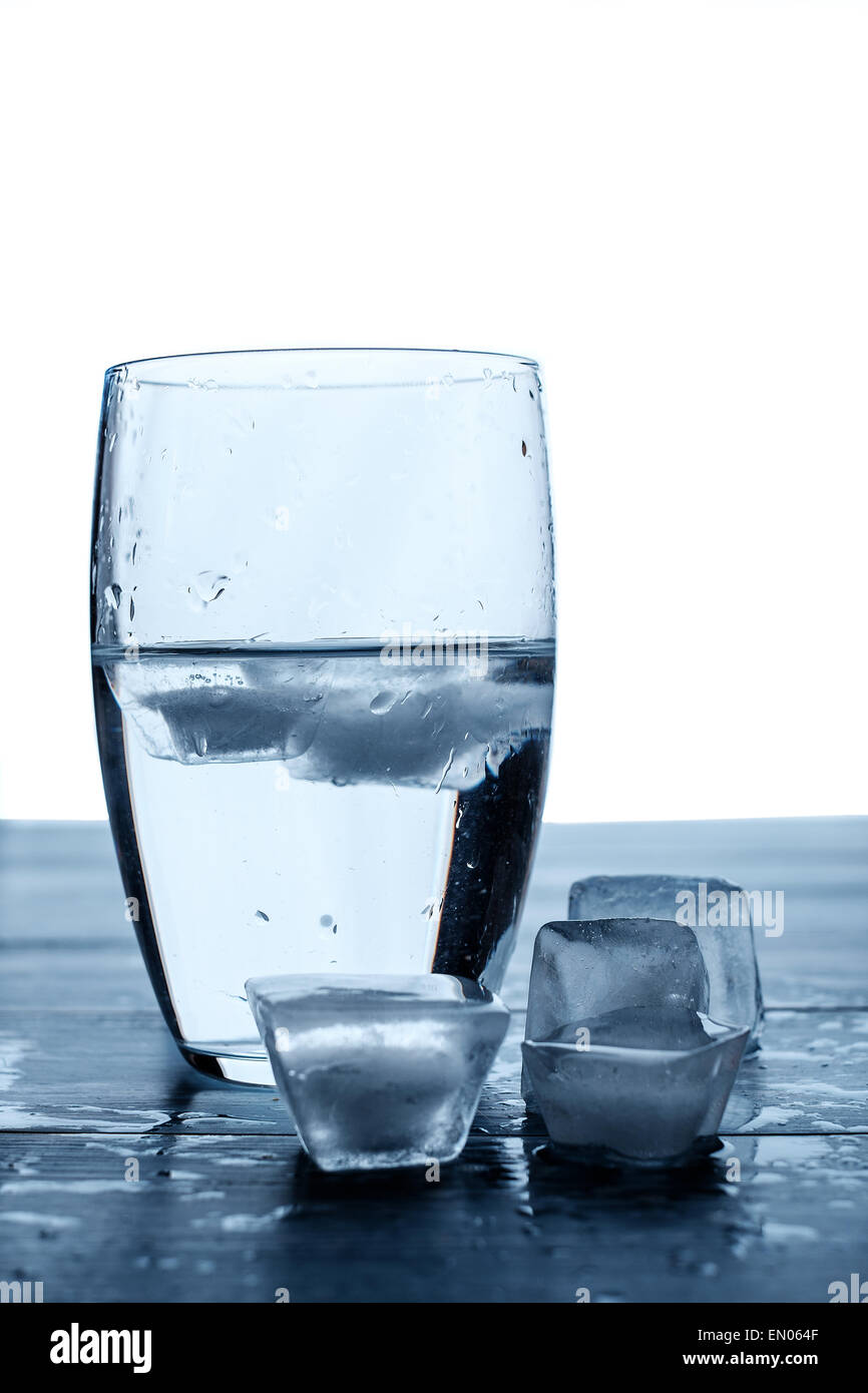 Glass of water and melting ice cubes on a wooden table Stock Photo - Alamy