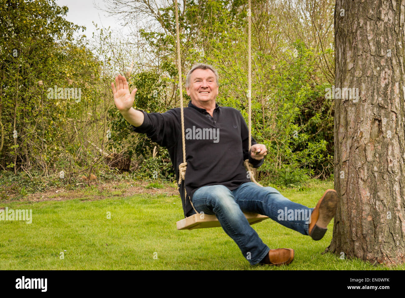 Senior man waving whilst on a tree swing in the garden Stock Photo - Alamy