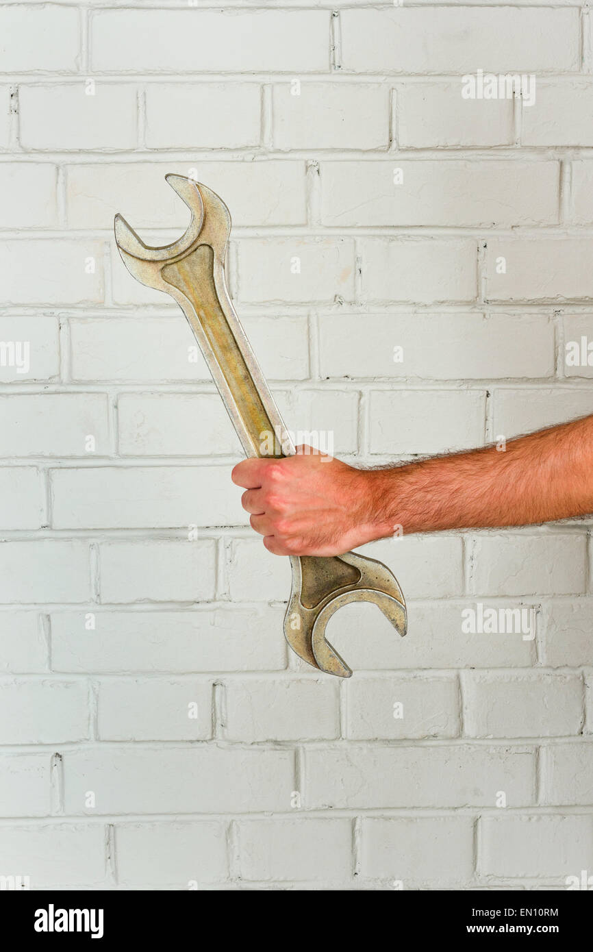 Man's hand with big spanner against white brick wall Stock Photo - Alamy