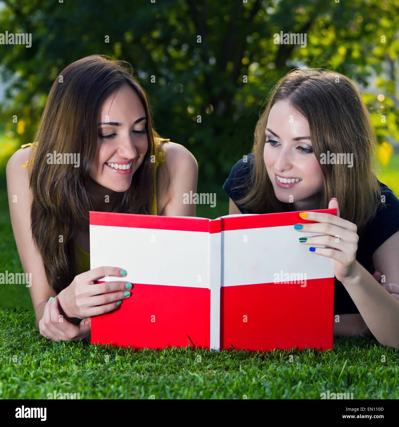 Two young happy smiling girls reading an open book in a summer g Stock ...