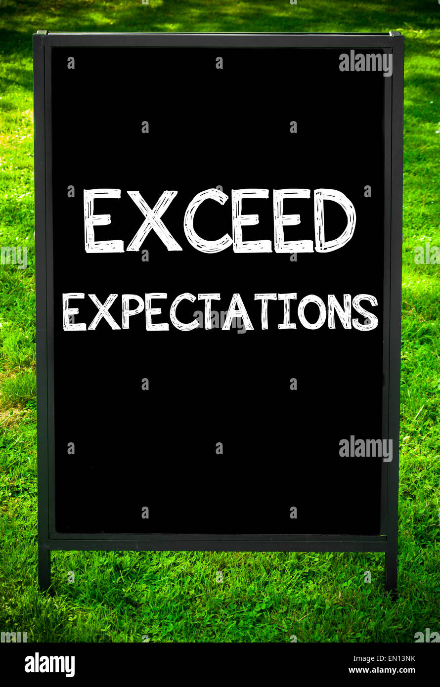 EXCEED EXPECTATIONS message on sidewalk blackboard sign against green ...