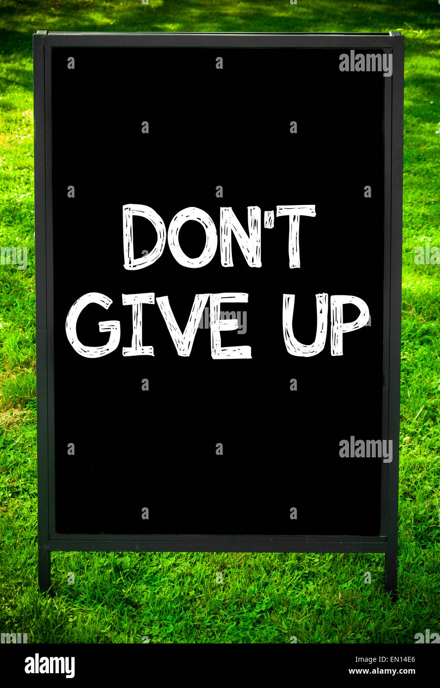 DON'T GIVE UP message on sidewalk blackboard sign against green grass ...