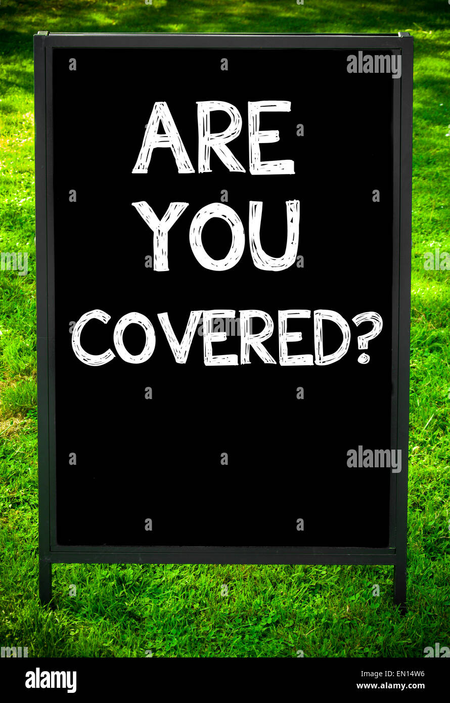 ARE YOU COVERED? message on sidewalk blackboard sign against green ...