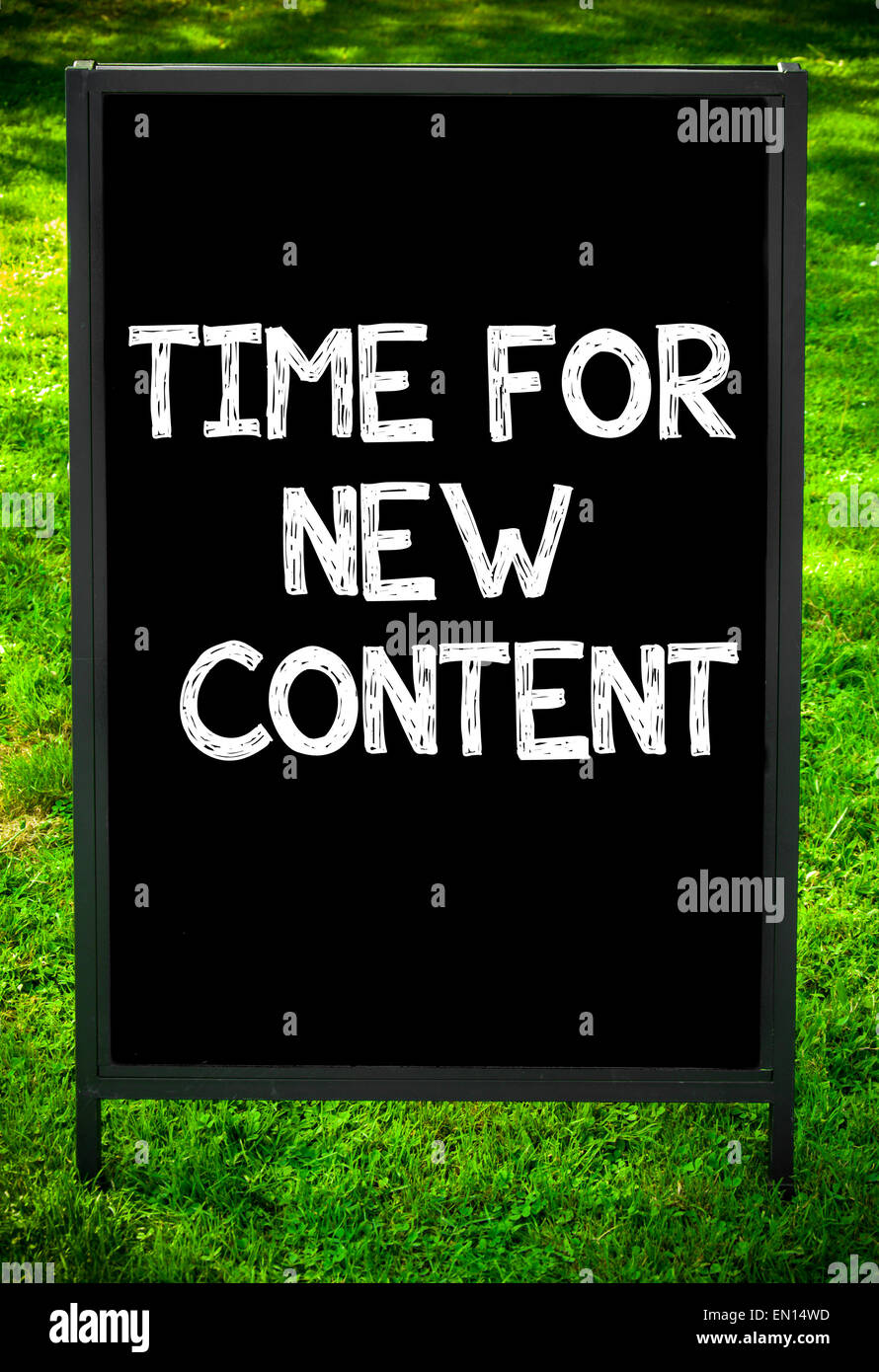 TIME FOR NEW CONTENT message on sidewalk blackboard sign against green ...