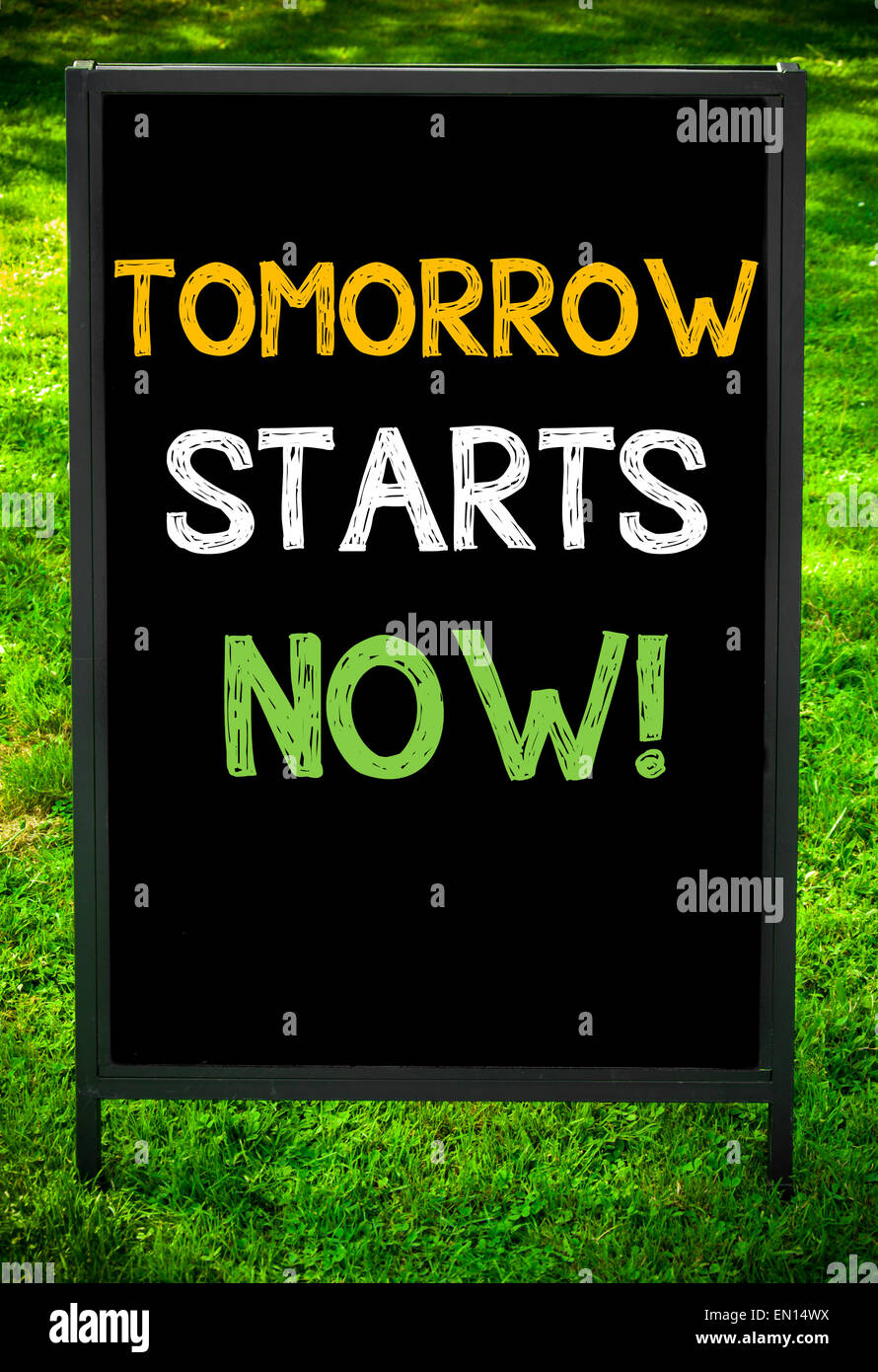 TOMORROW STARTS NOW! message on sidewalk blackboard sign against green ...