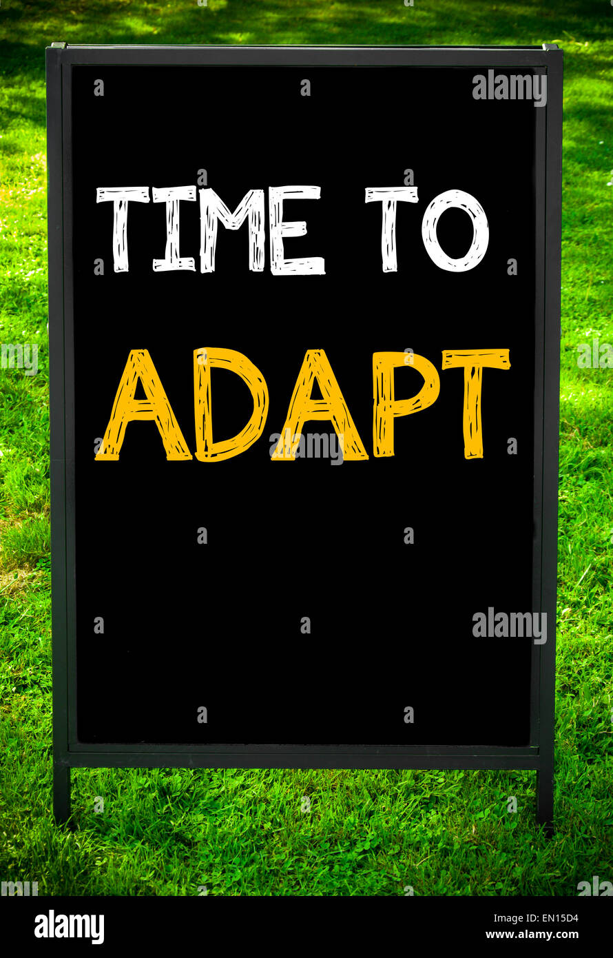 TIME TO ADAPT message on sidewalk blackboard sign against green grass ...