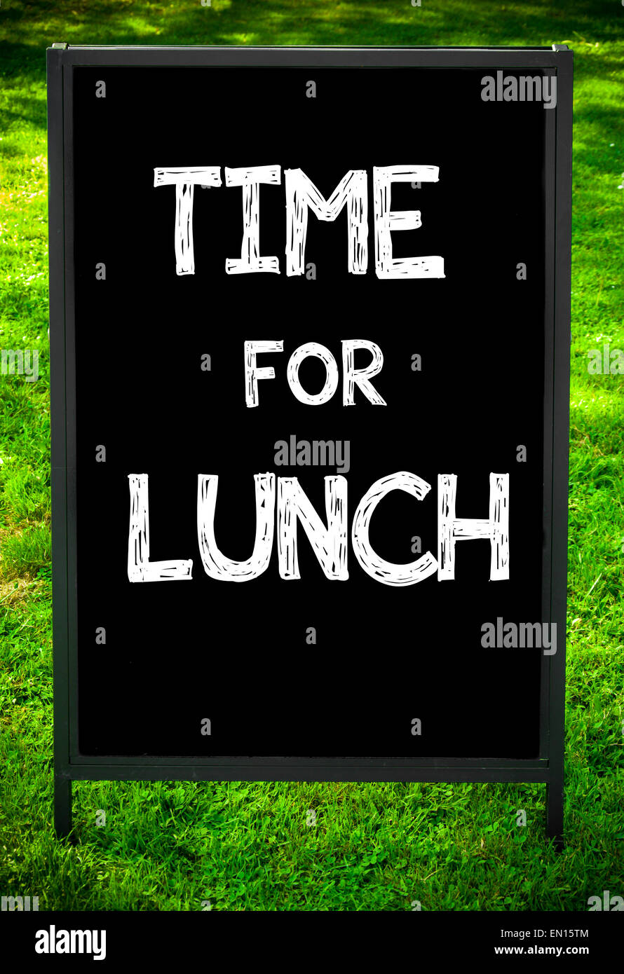 TIME FOR LUNCH message on sidewalk blackboard sign against green grass ...