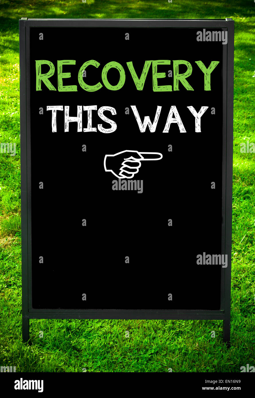 RECOVERY THIS WAY message on sidewalk blackboard sign against green ...