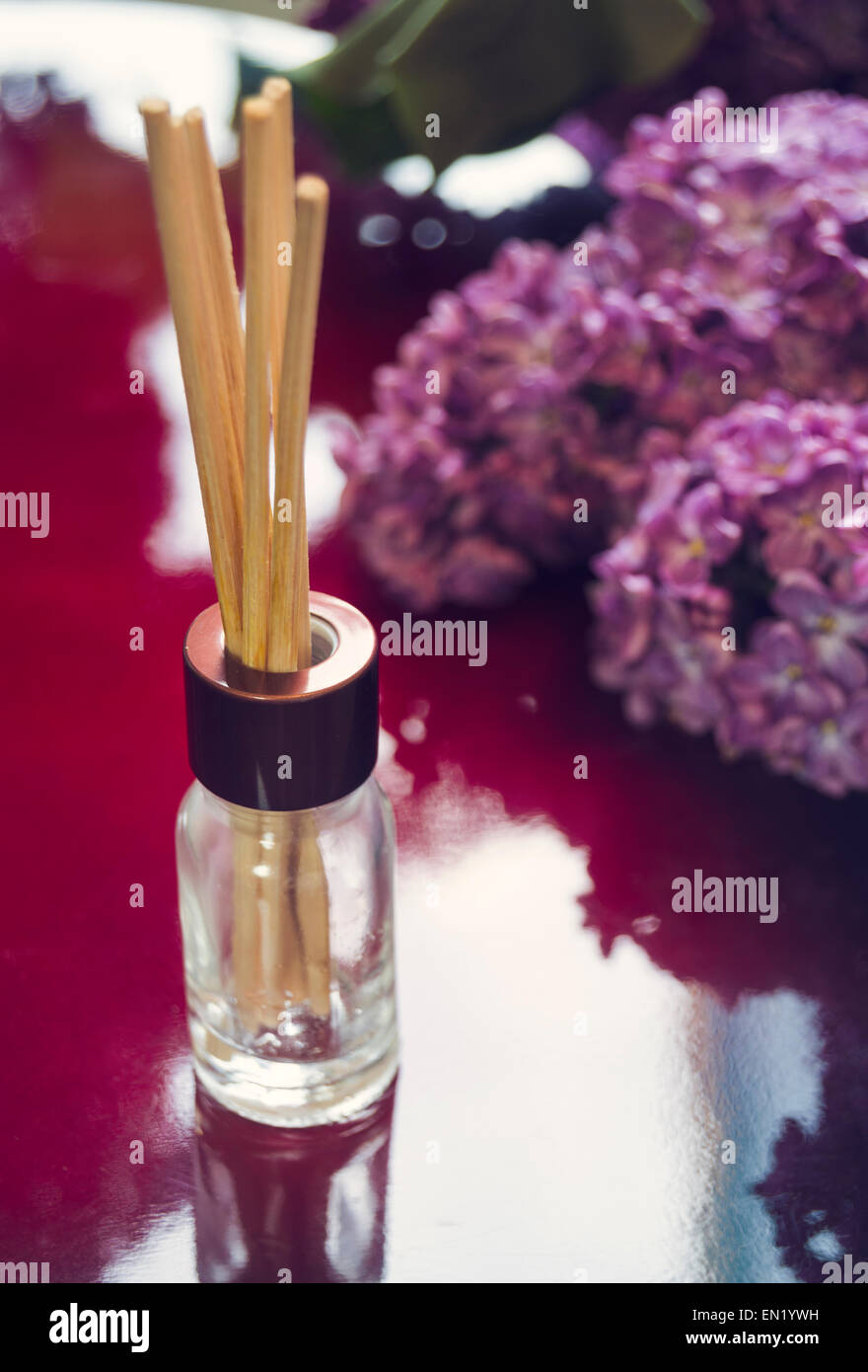 Aroma diffuser with bamboo sticks mounted and branches of lilac on red ...