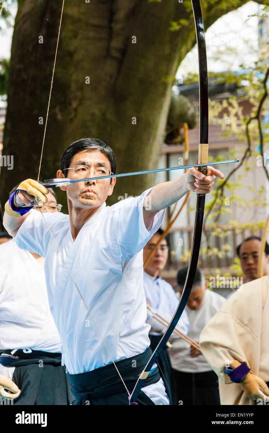 Japanese men standing in a row shooting arrows from bows at an archery ...