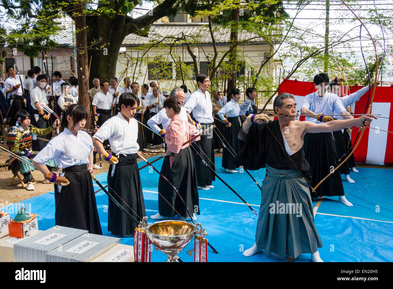 Japanese men standing in a row shooting arrows from bows at an archery ...
