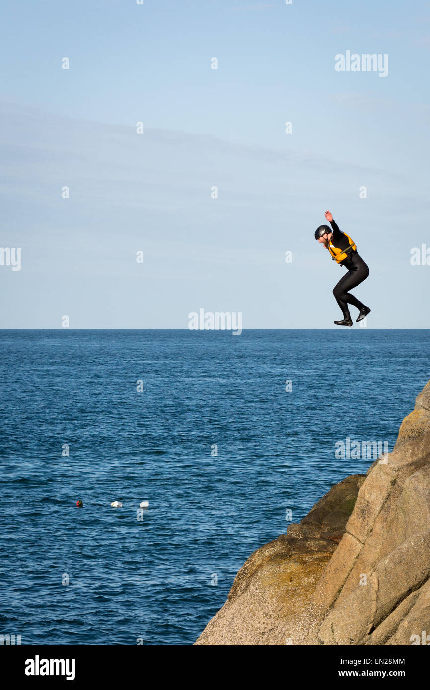 Man in wetsuit, helmet and lifejacket jumping off rocks into sea ...
