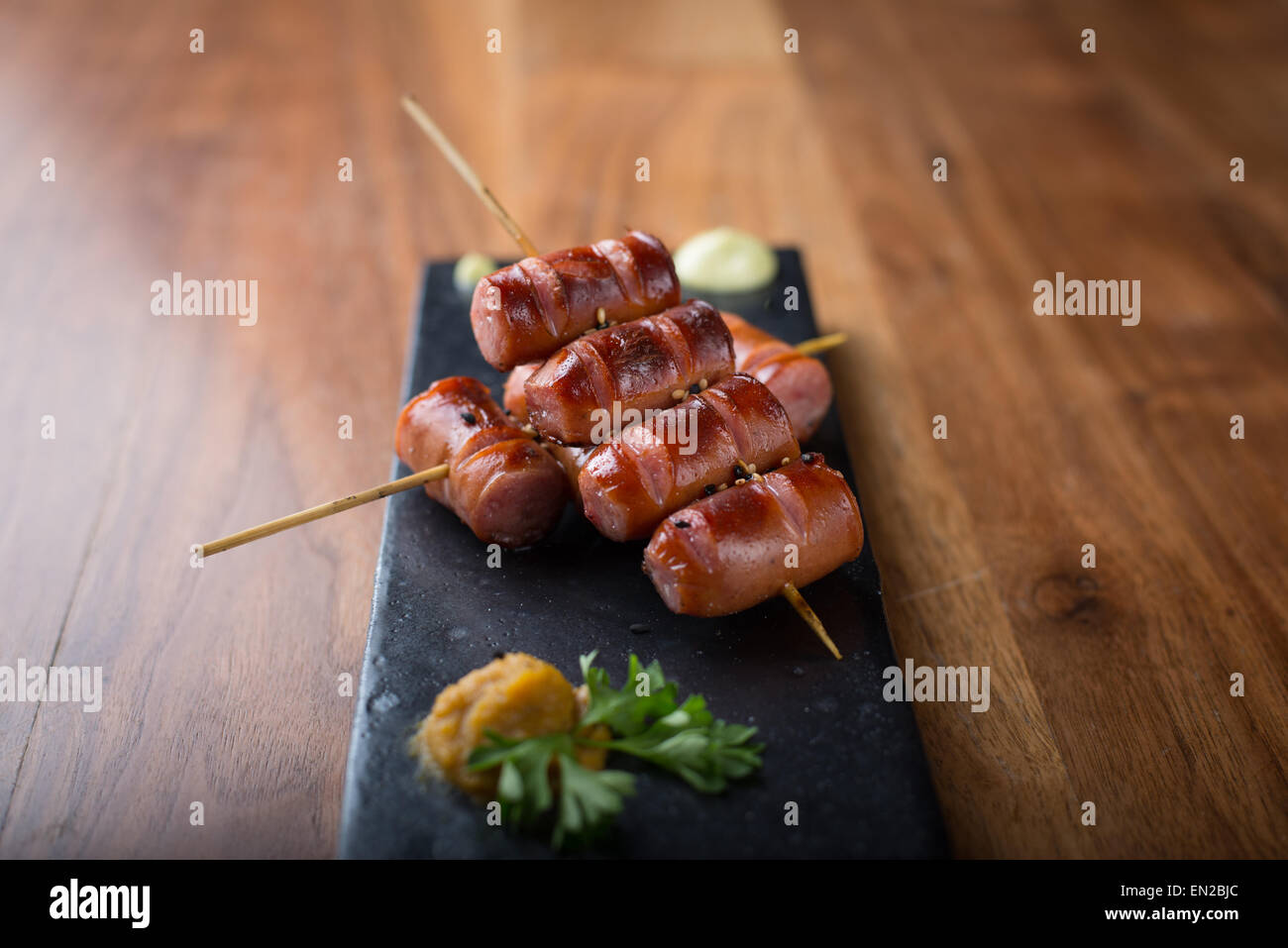 Skewered mini-sausage appetizer on black plate with wood table ...