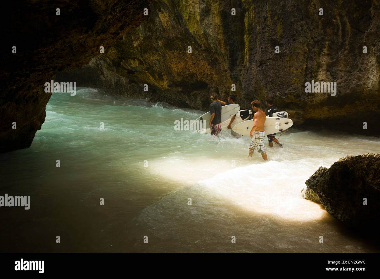 Surfers entering the sea through a cave at Uluwatu, Bali, Indonesia ...