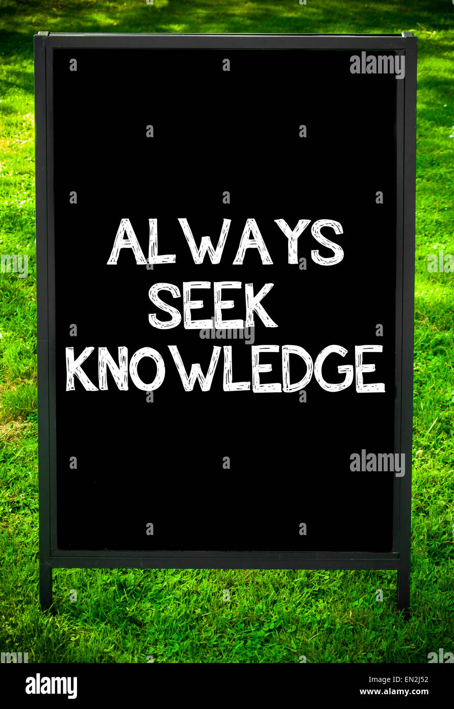 ALWAYS SEEK KNOWLEDGE message on sidewalk blackboard sign against green ...