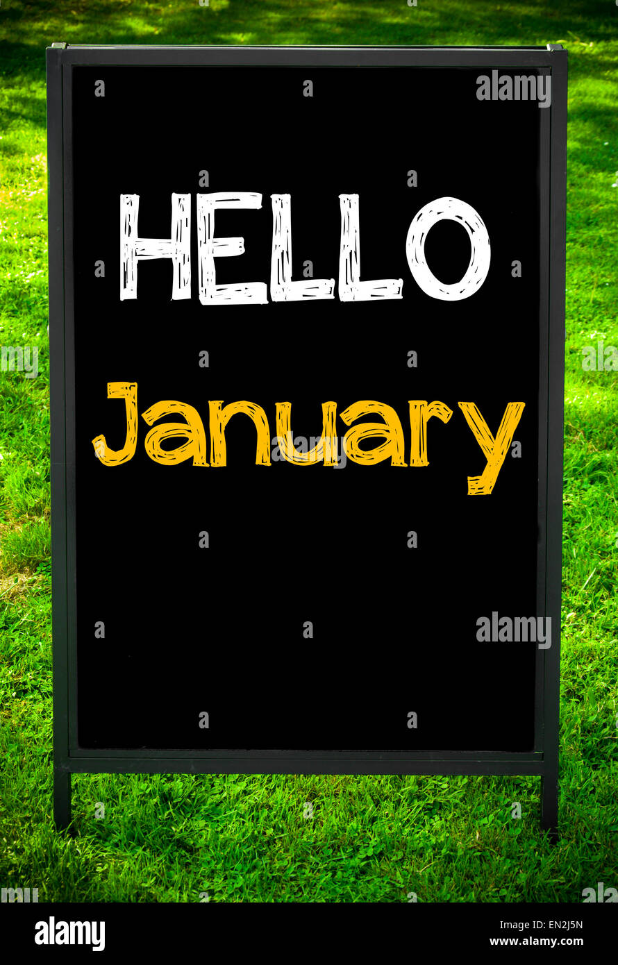 HELLO JANUARY message on sidewalk blackboard sign against green grass ...
