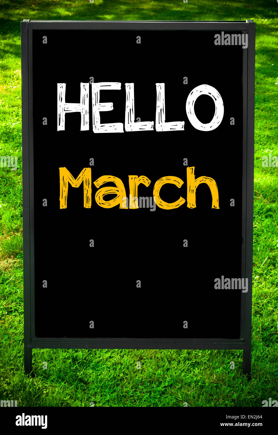 HELLO MARCH message on sidewalk blackboard sign against green grass ...