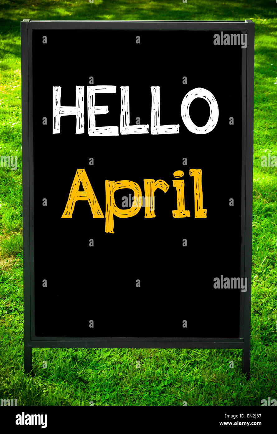 HELLO APRIL message on sidewalk blackboard sign against green grass ...