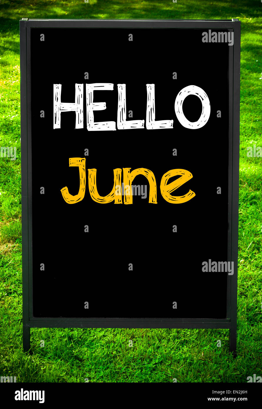 HELLO JUNE message on sidewalk blackboard sign against green grass ...