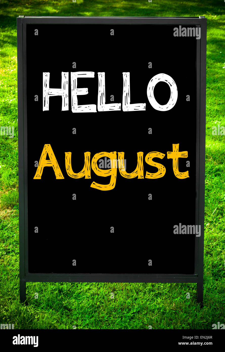 HELLO AUGUST message on sidewalk blackboard sign against green grass ...