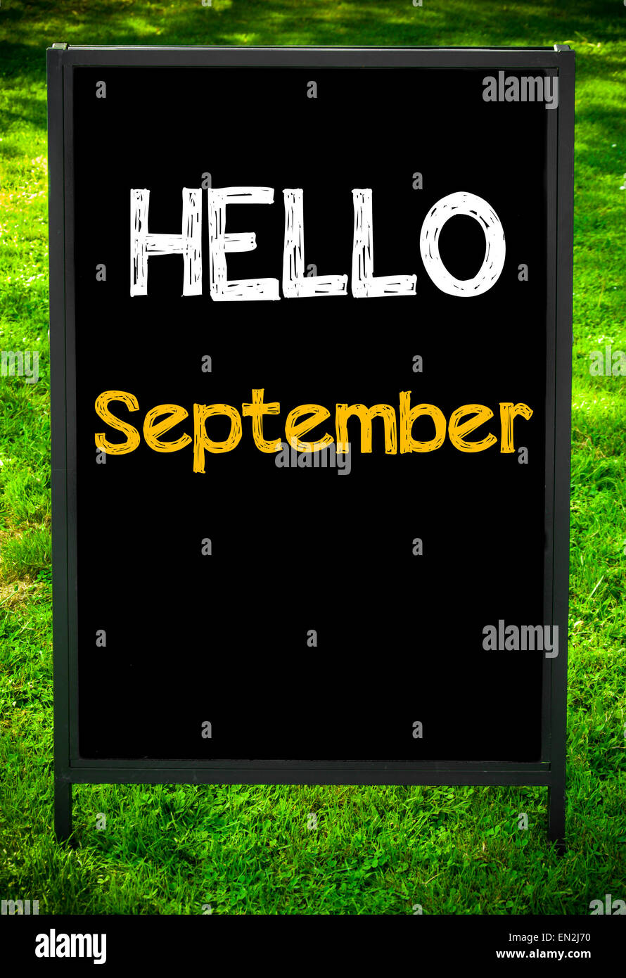 HELLO SEPTEMBER message on sidewalk blackboard sign against green grass ...