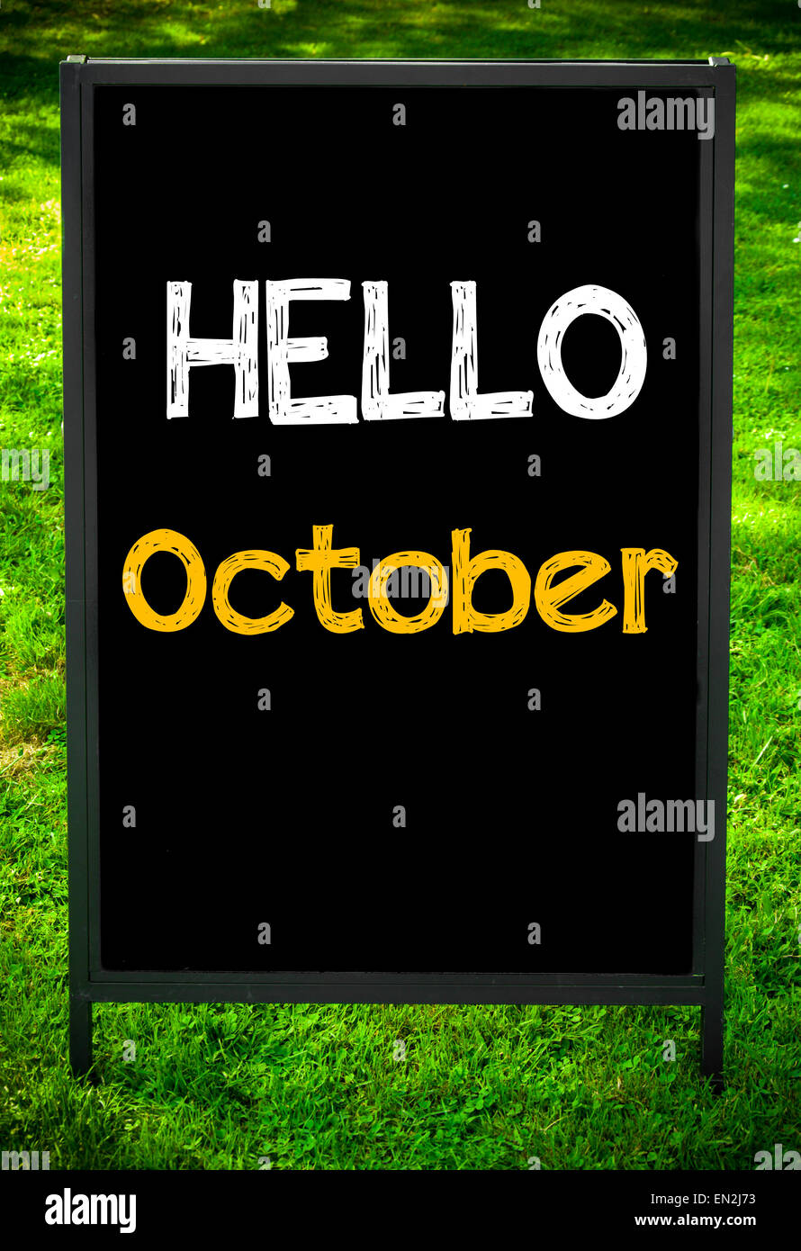 HELLO OCTOBER message on sidewalk blackboard sign against green grass ...