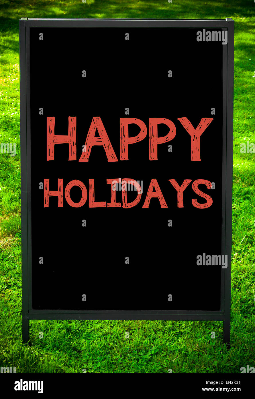 HAPPY HOLIDAYS message on sidewalk blackboard sign against green grass ...
