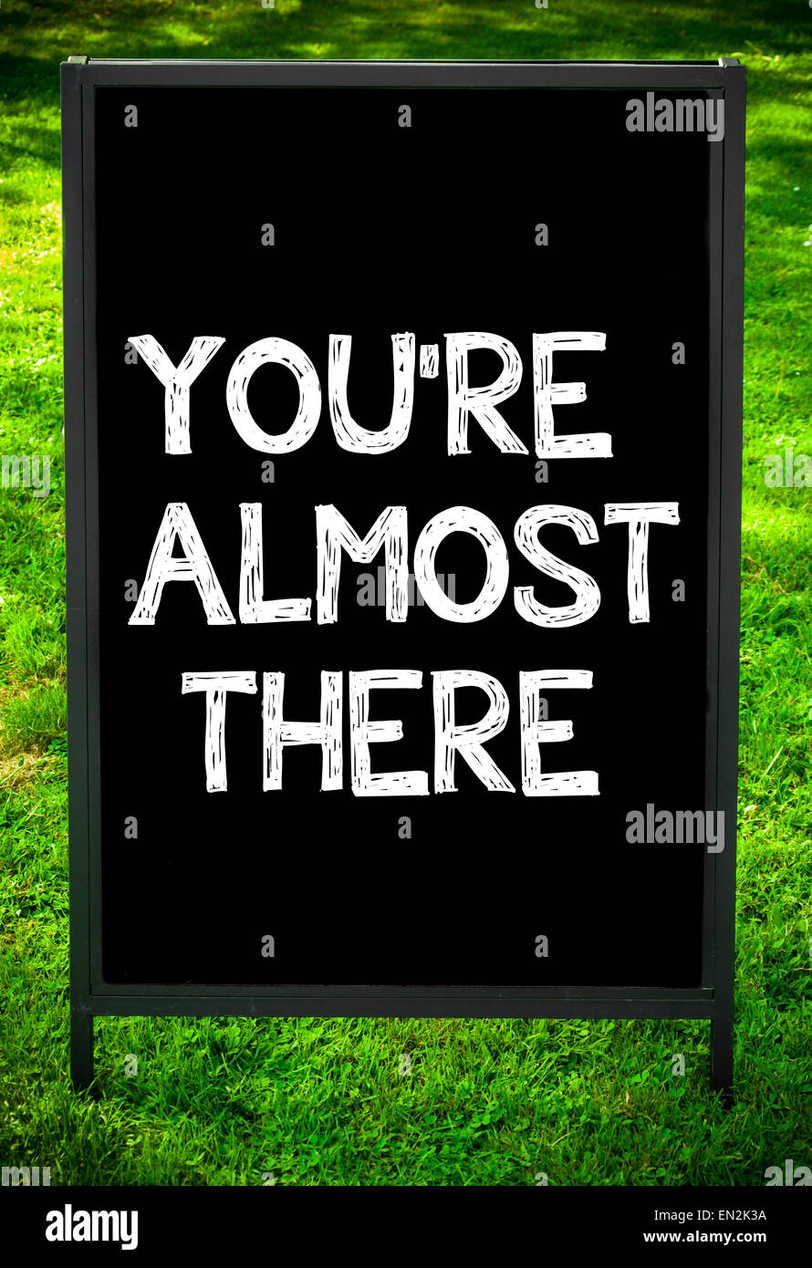 YOU'RE ALMOST THERE message on sidewalk blackboard sign against green ...
