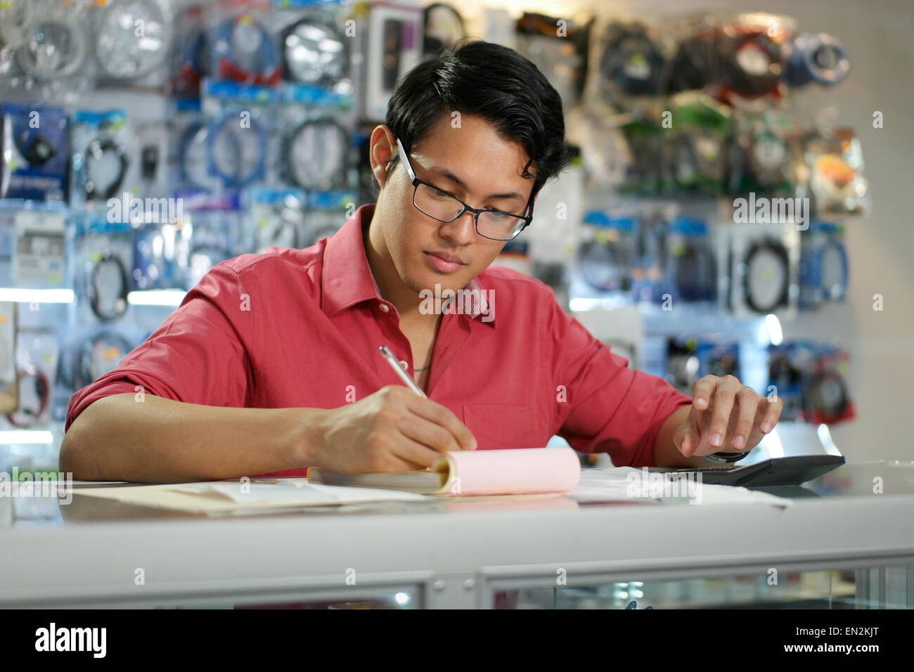 Young asian entrepreneur owning a computer shop and checking bills and ...