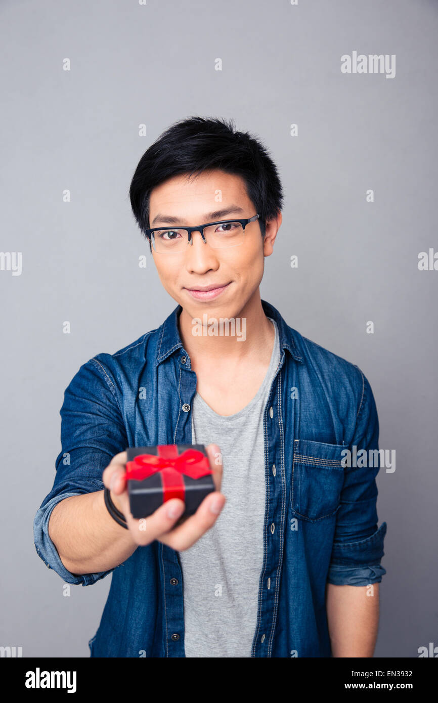 Happy young asian man giving gift box on the camera over gray ...