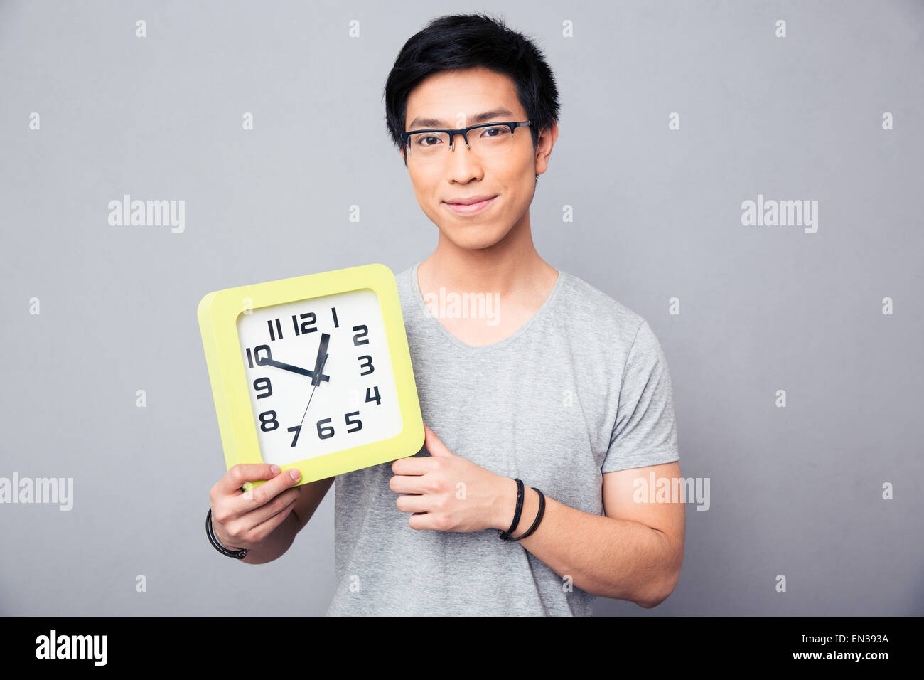 Happy asian man holding big clock over gray background and looking at ...