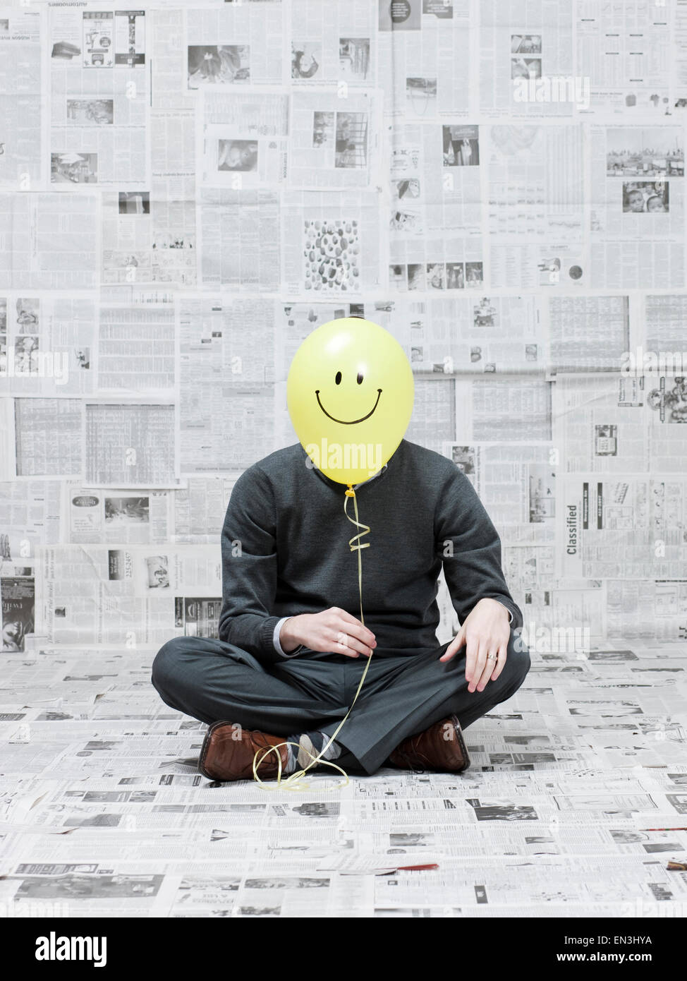 Studio shot of young man sitting and holding balloon face in front of ...
