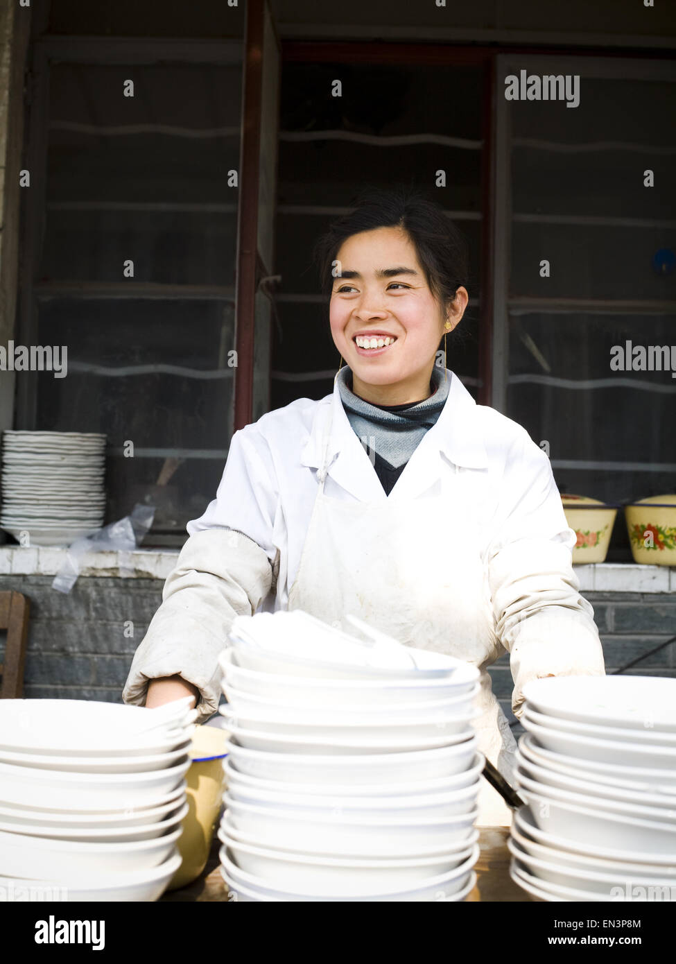 Woman standing with stacks of dishes smiling Stock Photo - Alamy