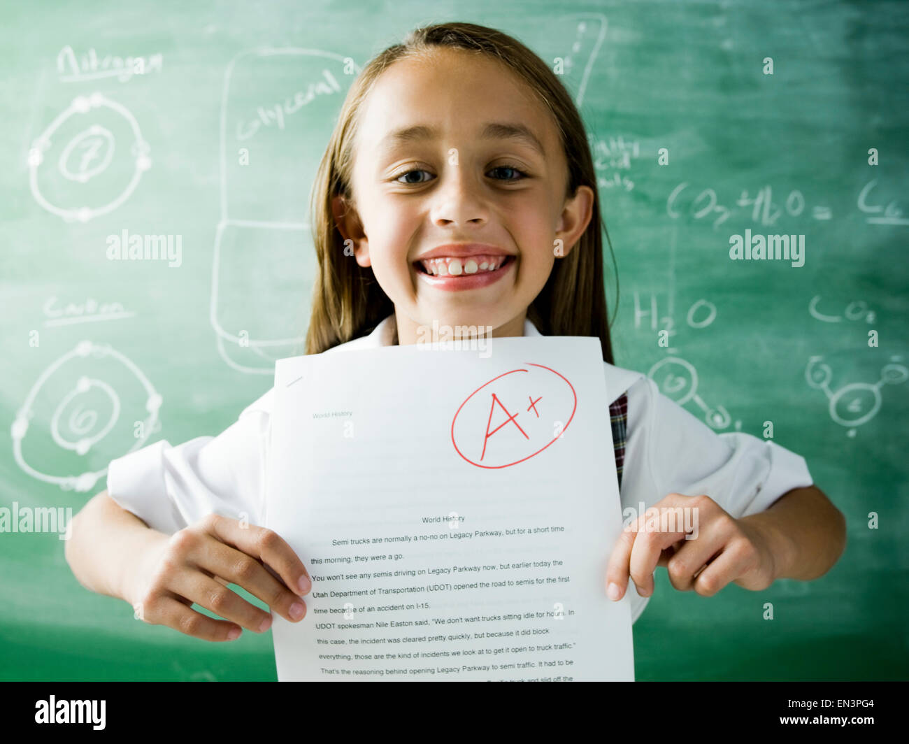 girl in a classroom holding up an a plus paper Stock Photo - Alamy