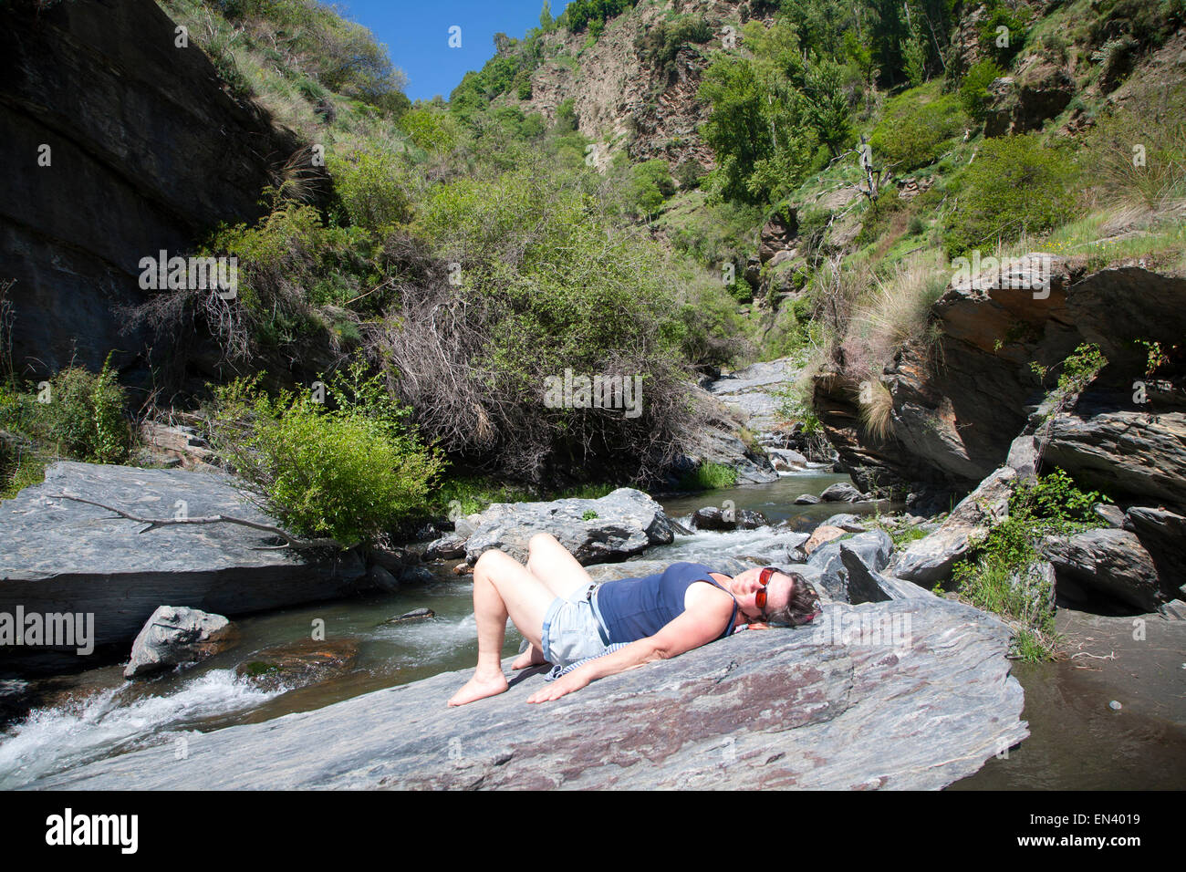 Woman sunbathing on rock by rapids in the channel of the River Rio ...