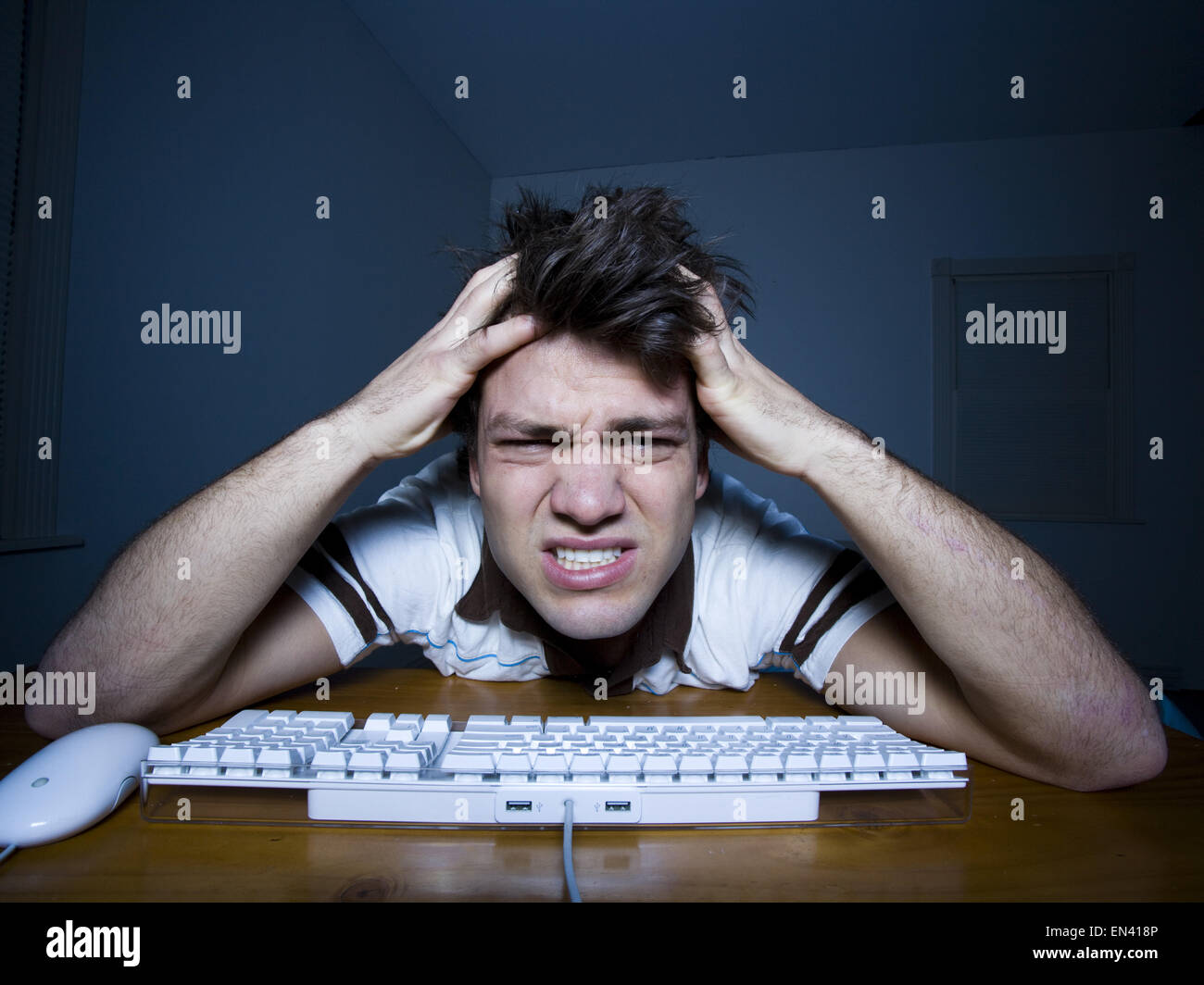 Man at keyboard with hands on head snarling Stock Photo - Alamy