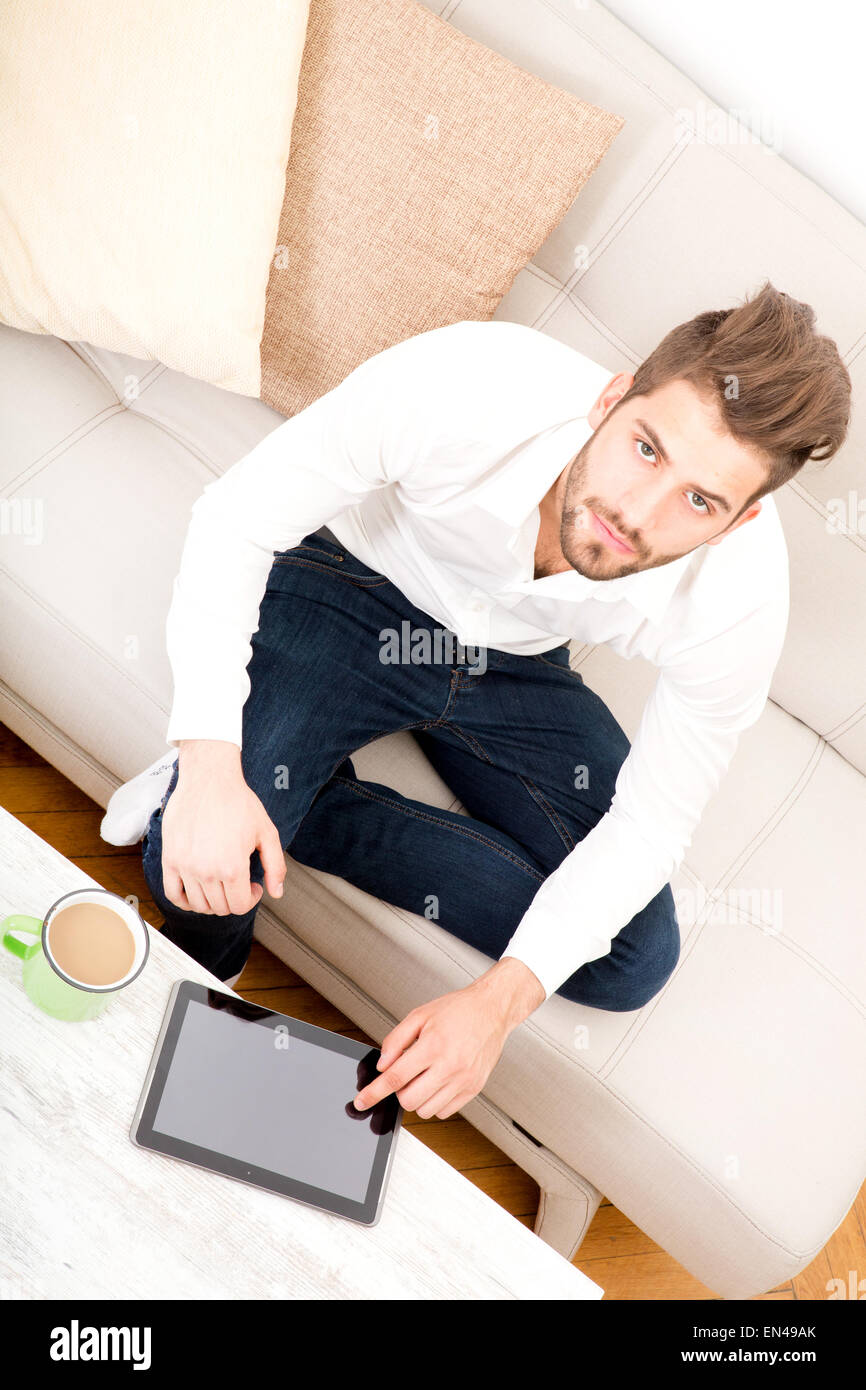 A young adult man sitting on the couch using a tablet Stock Photo - Alamy