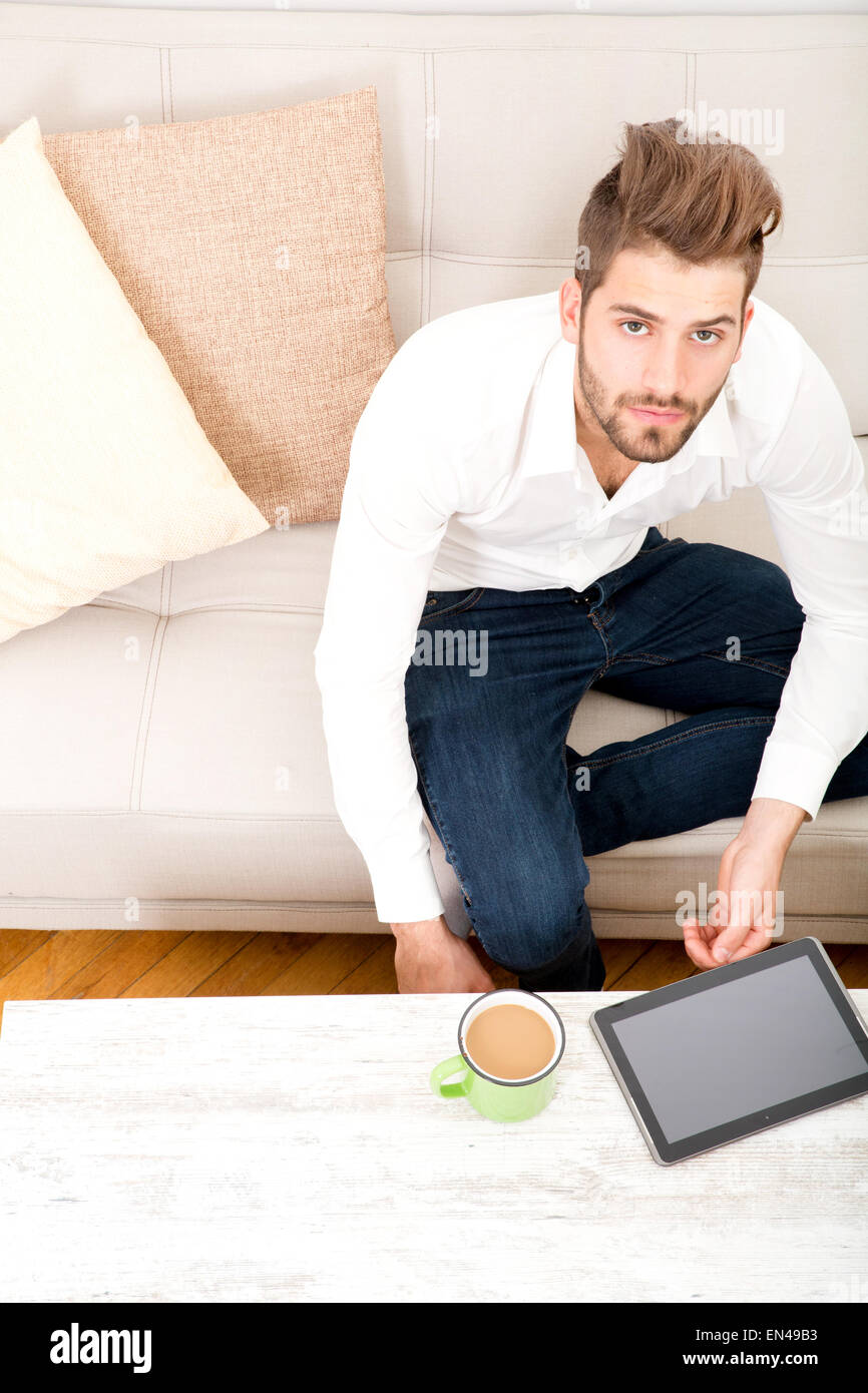 A young adult man sitting on the couch using a tablet Stock Photo - Alamy