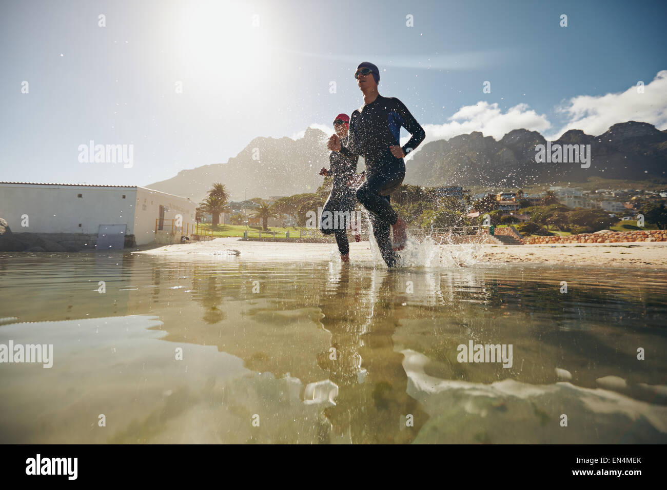 Two competitors in wet suits running into the water at the start of a ...