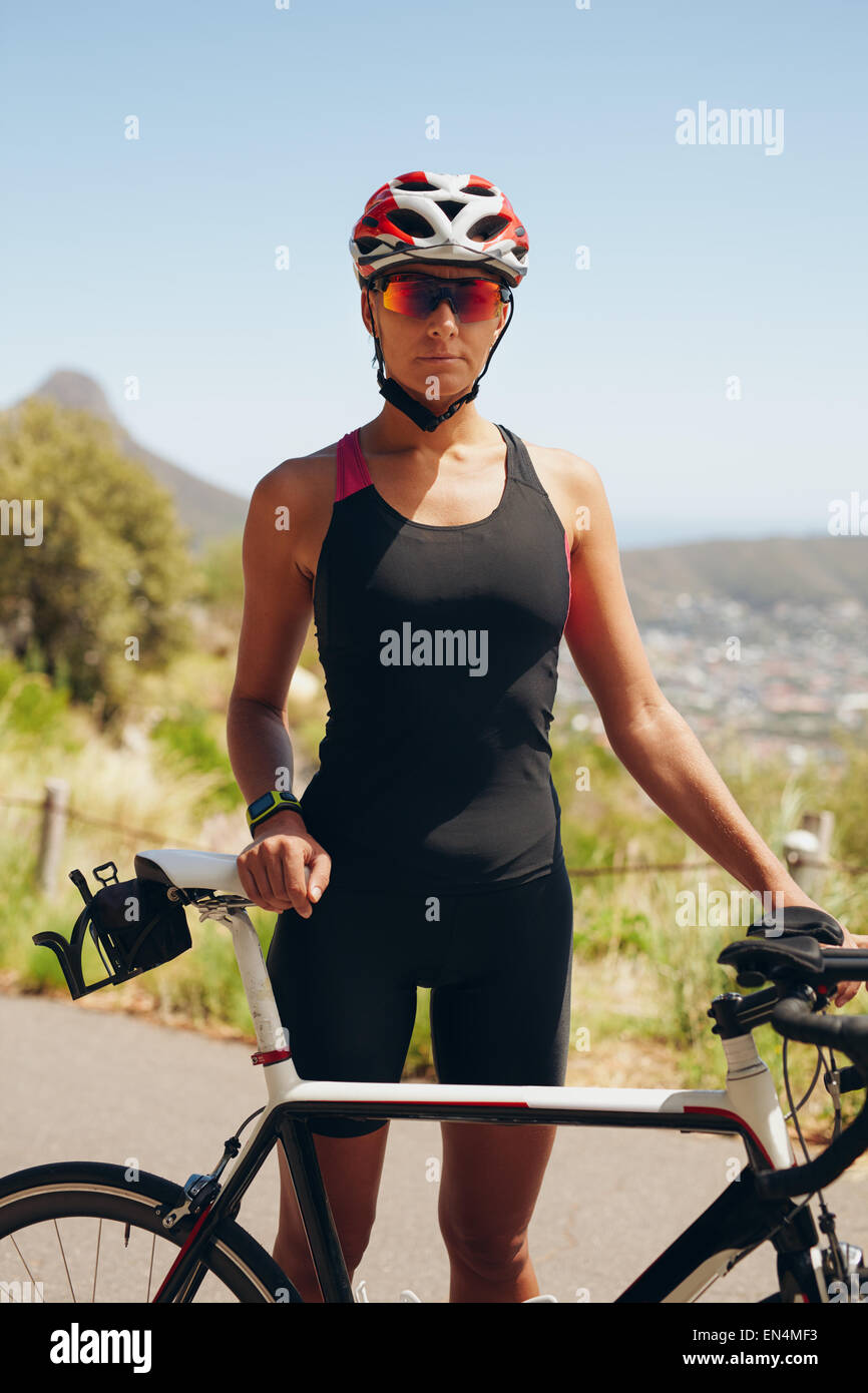 Portrait of confident female triathlete standing with her bicycle on ...