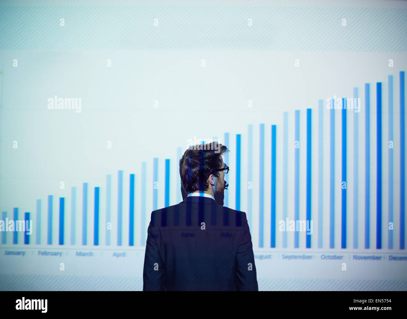 Rear view of businessman standing by wall and looking at chart on it ...