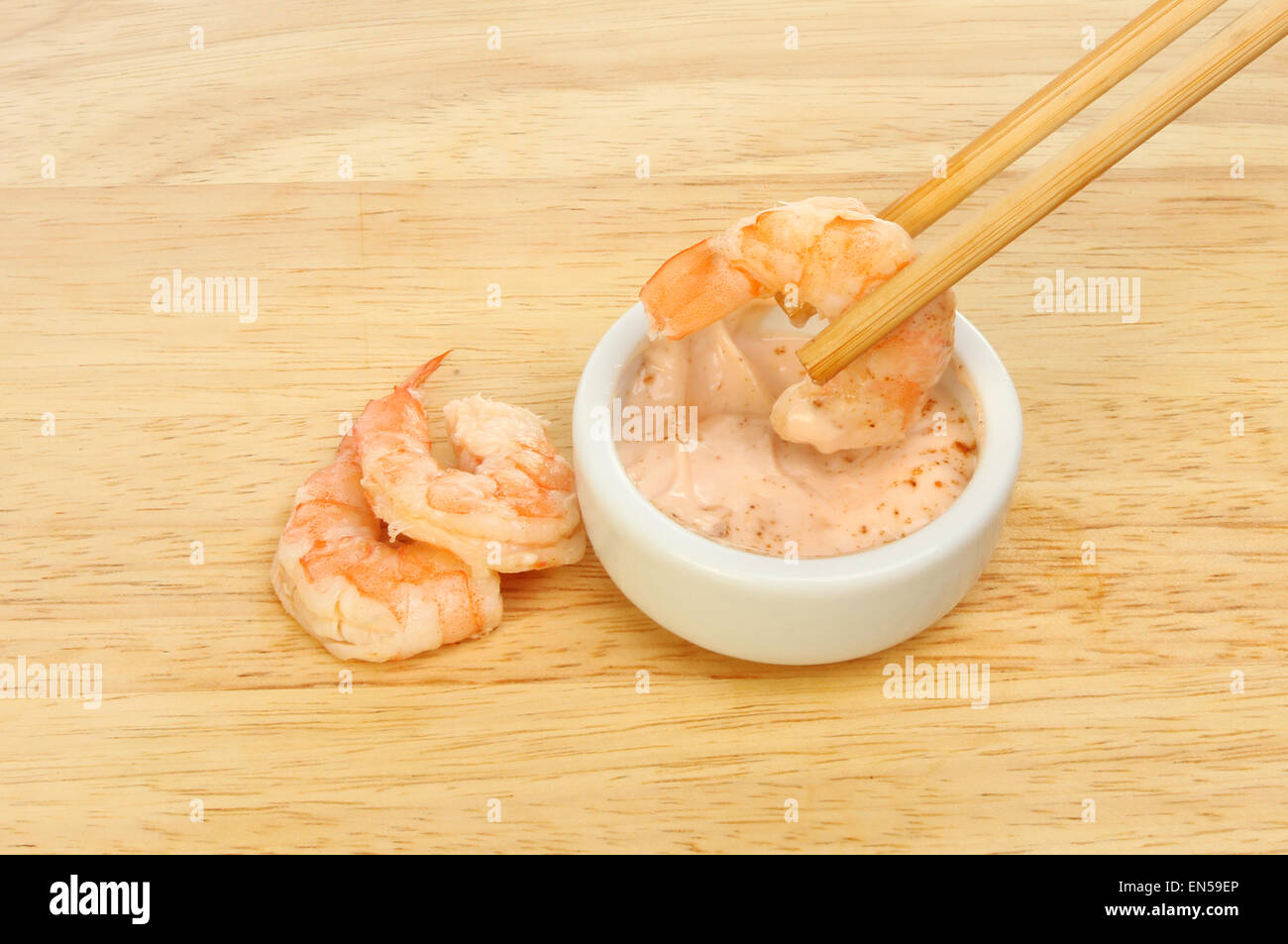 Prawn in chopsticks dipping in seafood sauce with two prawns on a ...