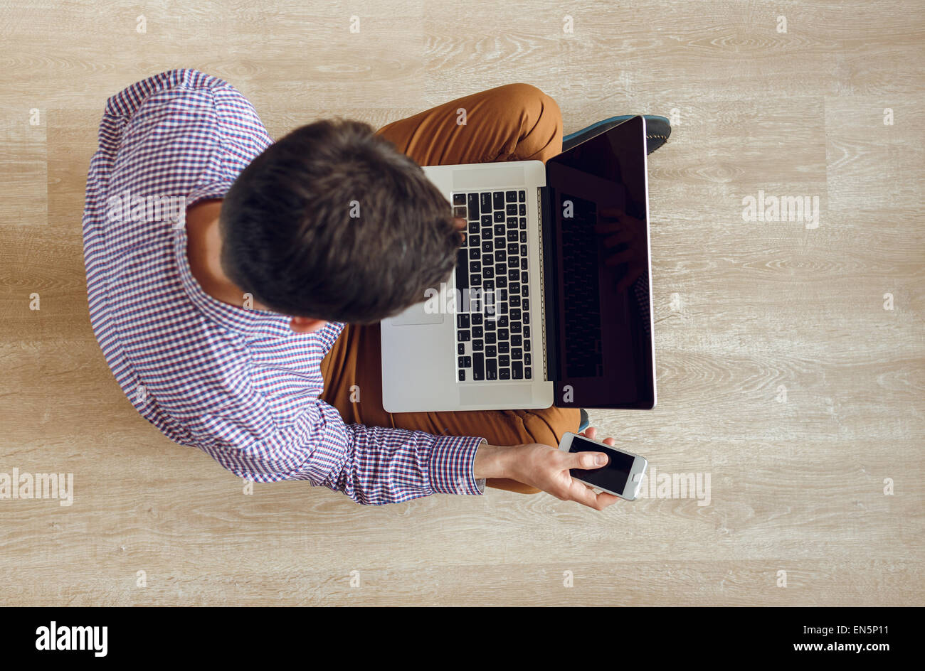 Top view of young man sitting on the floor and working with a laptop ...