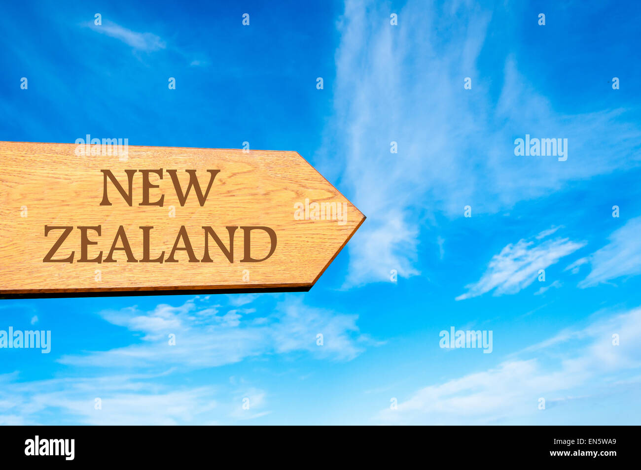 Wooden arrow sign pointing destination NEW ZEALAND against clear blue ...