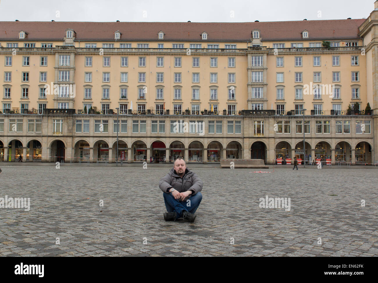 The man in a gray jacket and jeans sits in the middle of a city square ...