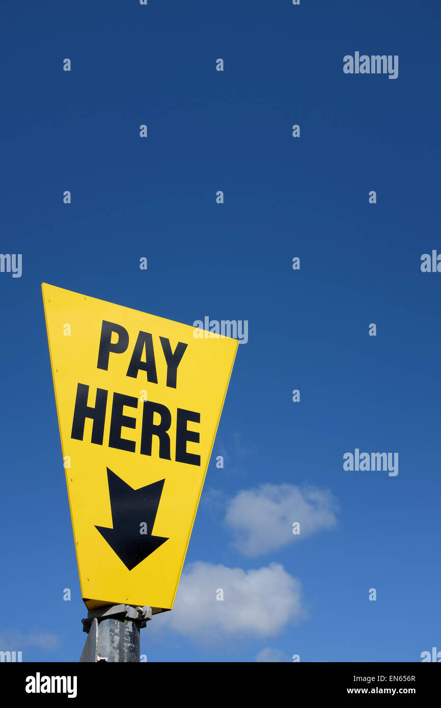 Yellow pay here sign against a blue sky background with copy space ...